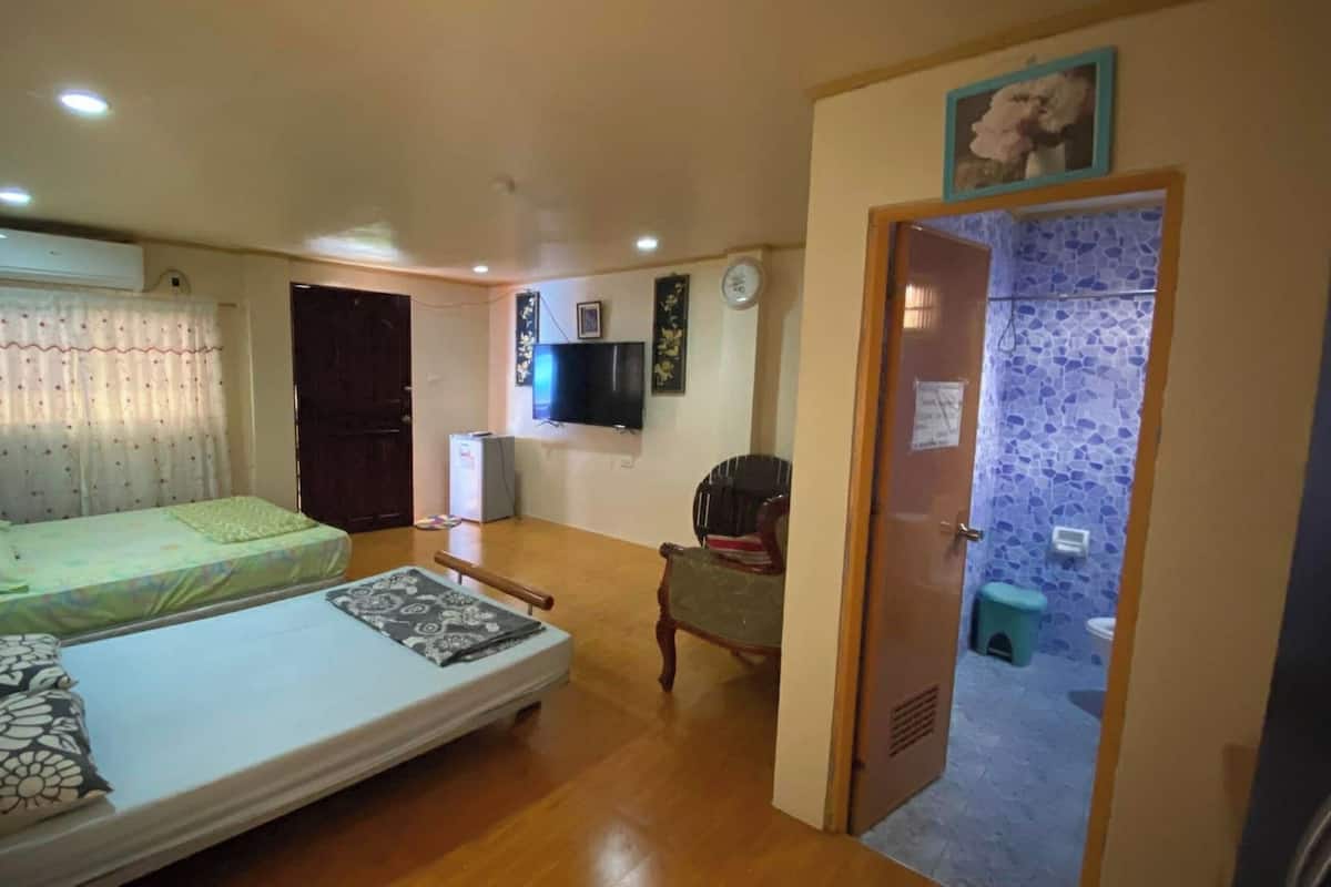 Quarto com duas camas, televisão, relógio e banheiro com parede revestida de azulejos.