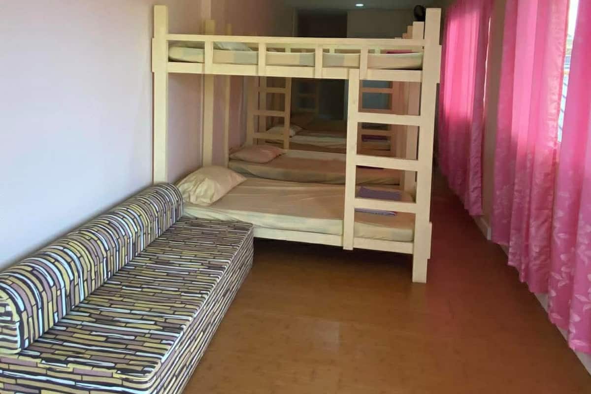 Quarto com beliche, sofá, piso de madeira e cortinas cor de rosa.