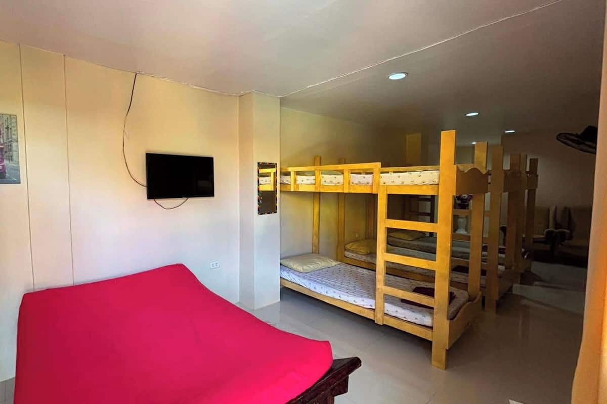 Quarto com beliches, uma cadeira vermelha, televisão de tela plana e prateleira na parede.