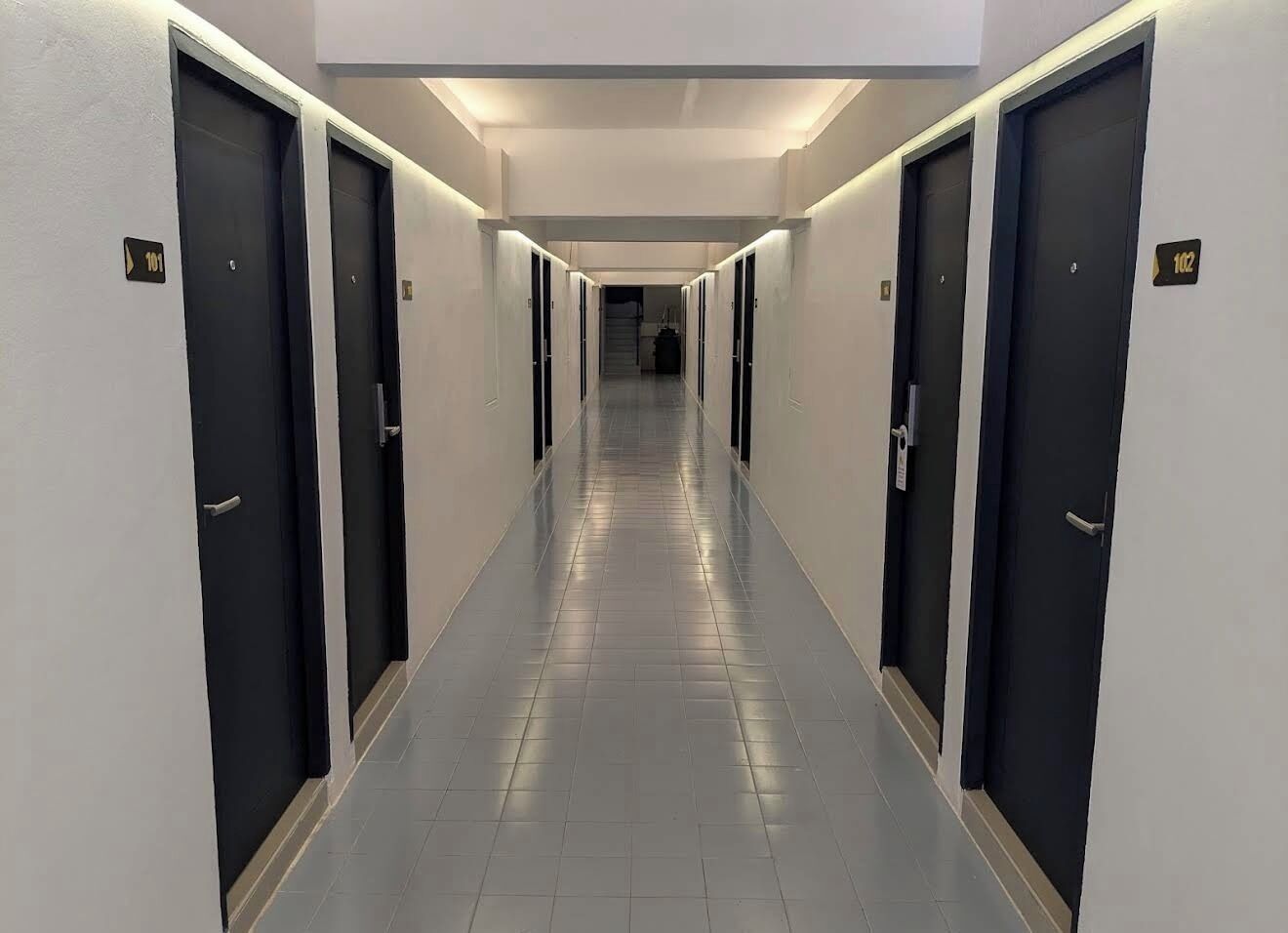 Corredor longo e estreito de hotel com portas numeradas 101 e 102, dando acesso aos quartos.