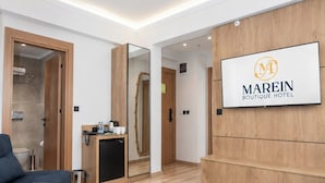 Quarto de hotel moderno com piso de madeira, um sofá, uma mesa de centro, um minibar e uma placa indicativa do Marein Boutique Hotel.