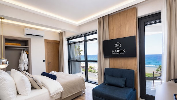 Quarto de hotel moderno com cama, área de estar, televisão e uma grande janela com vista para o mar.