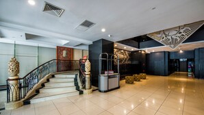 Um hall amplo com uma escadaria imponente, um balcão de atendimento e um teto decorativo.