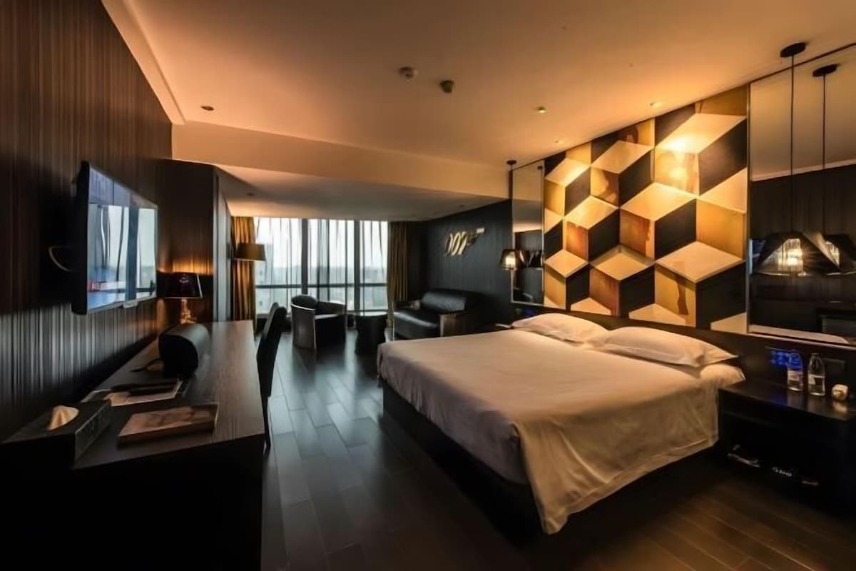 Quarto de hotel moderno com cama, escrivaninha, cadeira e uma grande janela.