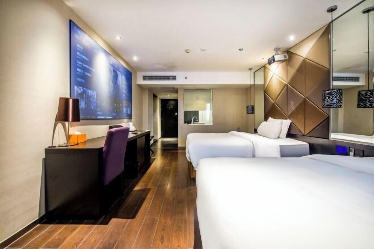Quarto de hotel moderno com duas camas, uma escrivaninha com cadeira, uma TV de tela plana grande e um espelho grande.