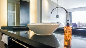Uma casa de banho moderna com um espelho grande, um lavatório branco e um frasco de gel desinfetante no balcão.