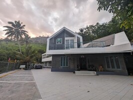 Um edifício de dois andares com varanda, garagem coberta e área de entrada pavimentada.