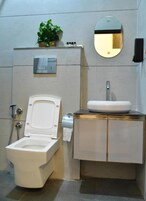 Casa de banho moderna com sanita, lavatório, espelho e uma pequena planta na parede.