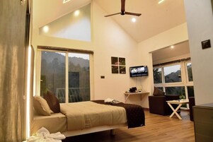 Quarto com cama, escrivaninha, televisão e vista para o exterior.