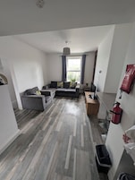 Uma sala de estar moderna com um sofá cinza, piso de madeira e uma janela com cortinas.