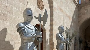 Duas estátuas de cavaleiros num pátio com paredes de pedra e uma porta em arco.
