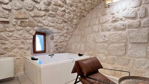 Um espaço de spa com parede de pedra, mesa de massagem, uma cadeira e uma mesinha com abajur.