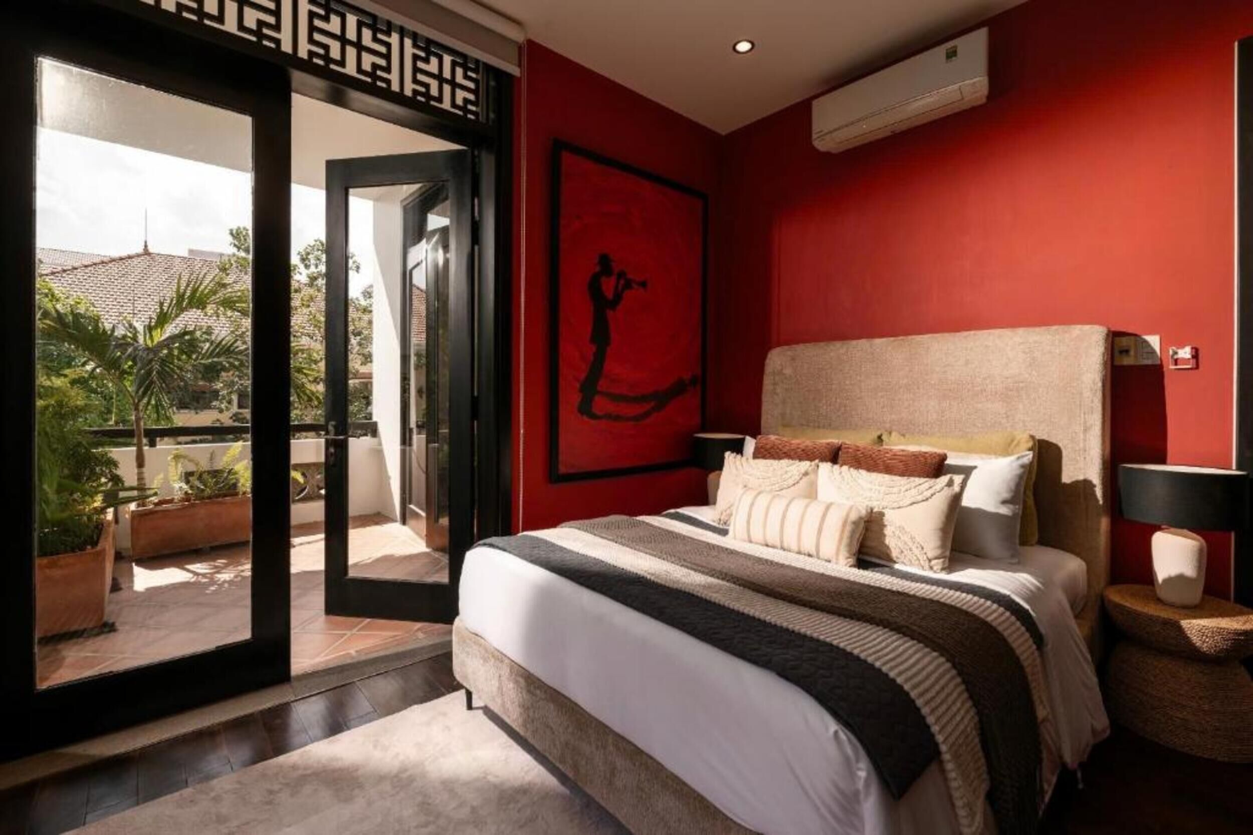 Quarto com uma cama grande, parede vermelha e vista para o exterior.