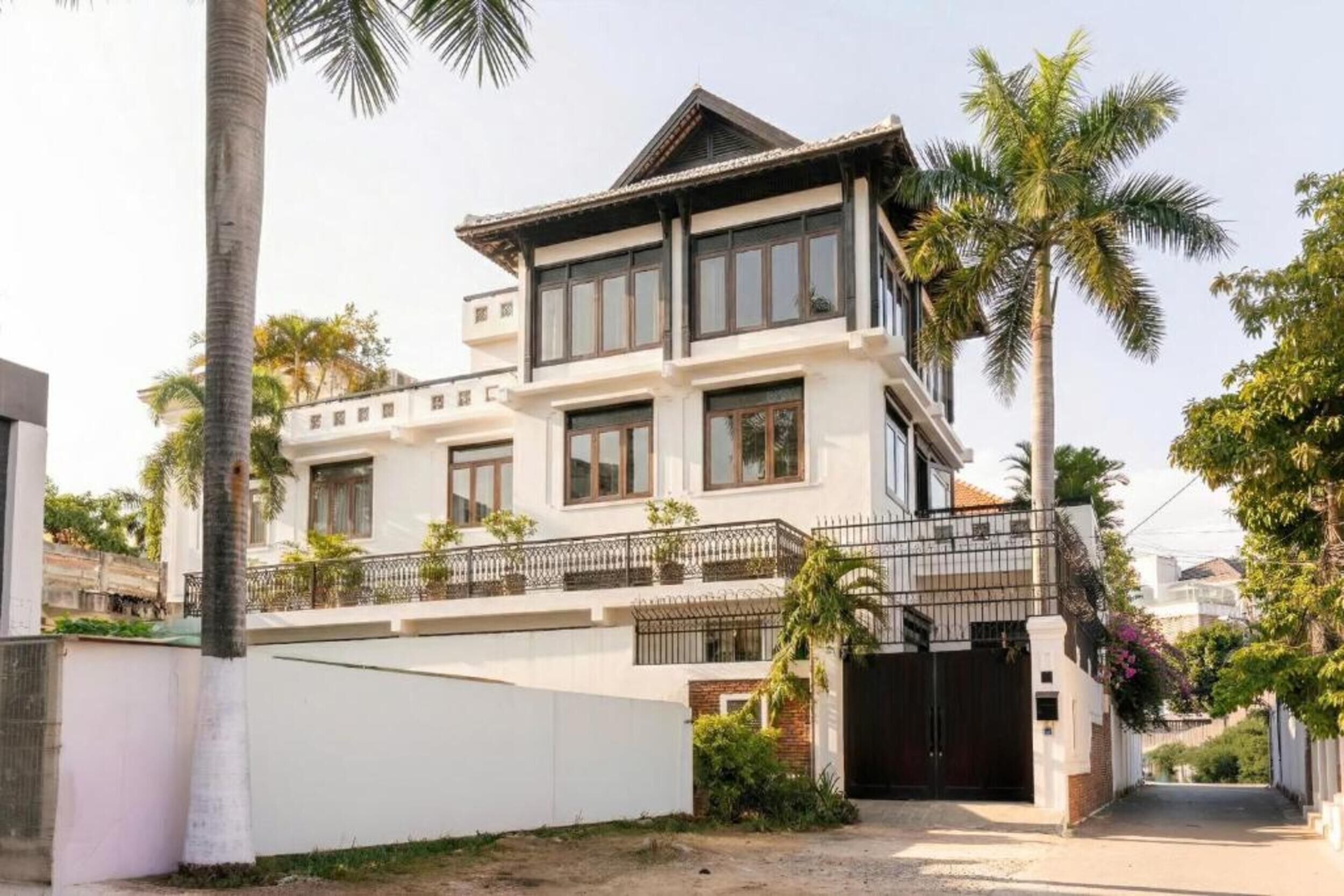 Uma casa de dois andares com varanda, portão e palmeiras.