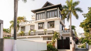 Uma casa de dois andares com varanda, portão e palmeiras.