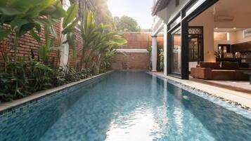 Piscina com borda revestida em azulejo, rodeada por vegetação e um muro de tijolos.