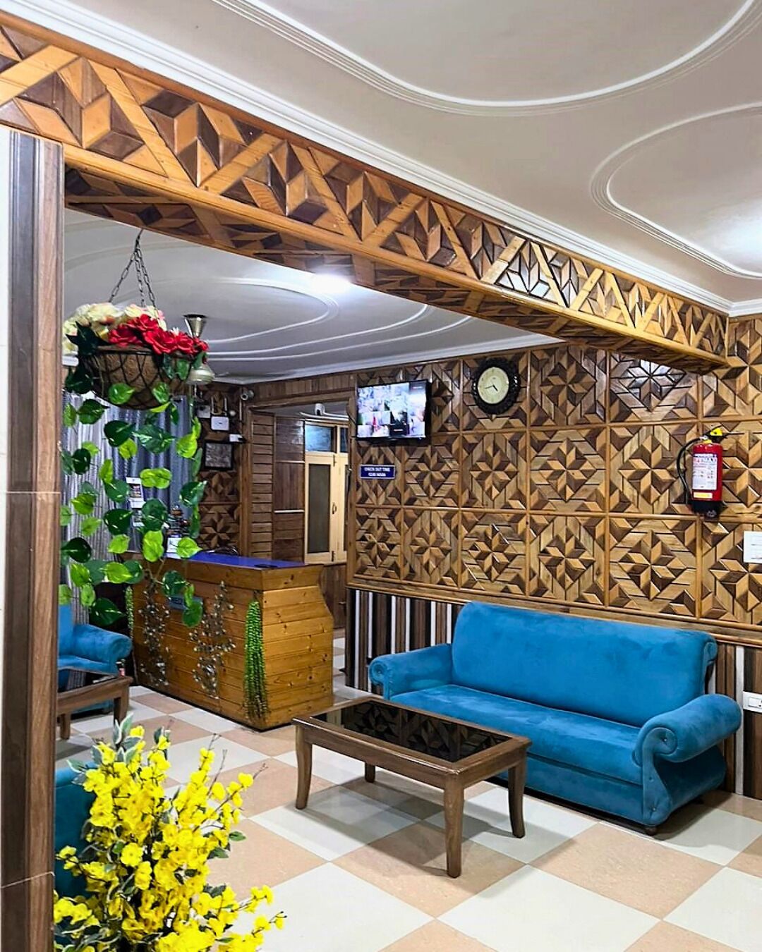 Uma área de recepção com sofá azul, painel de parede de madeira, balcão de recepção, plantas pendentes e um relógio.
