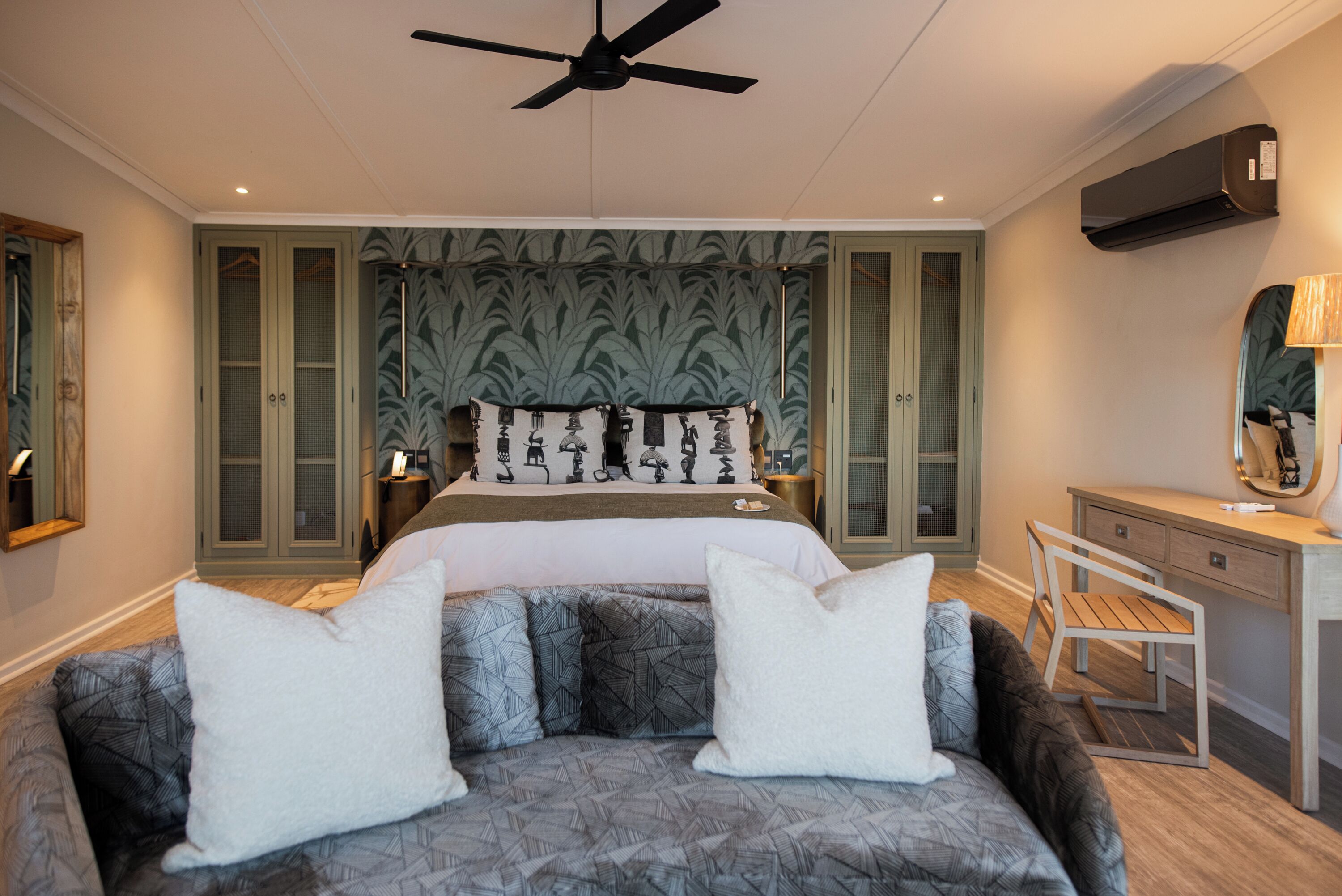 Quarto com cama, escrivaninha, cadeira, ventoinha no teto e guarda-roupa.