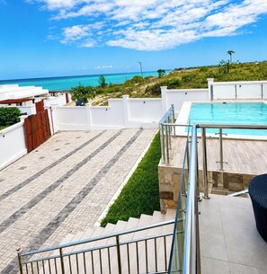 Uma piscina no terraço com vista clara para o oceano, um terraço em mosaico e uma escadaria que dá acesso à área da piscina.