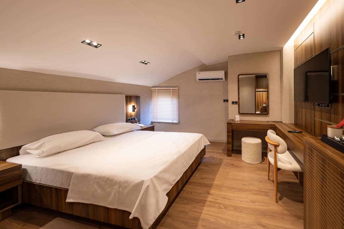 Quarto com cama, mesa de cabeceira, abajur, penteadeira, espelho e televisão.