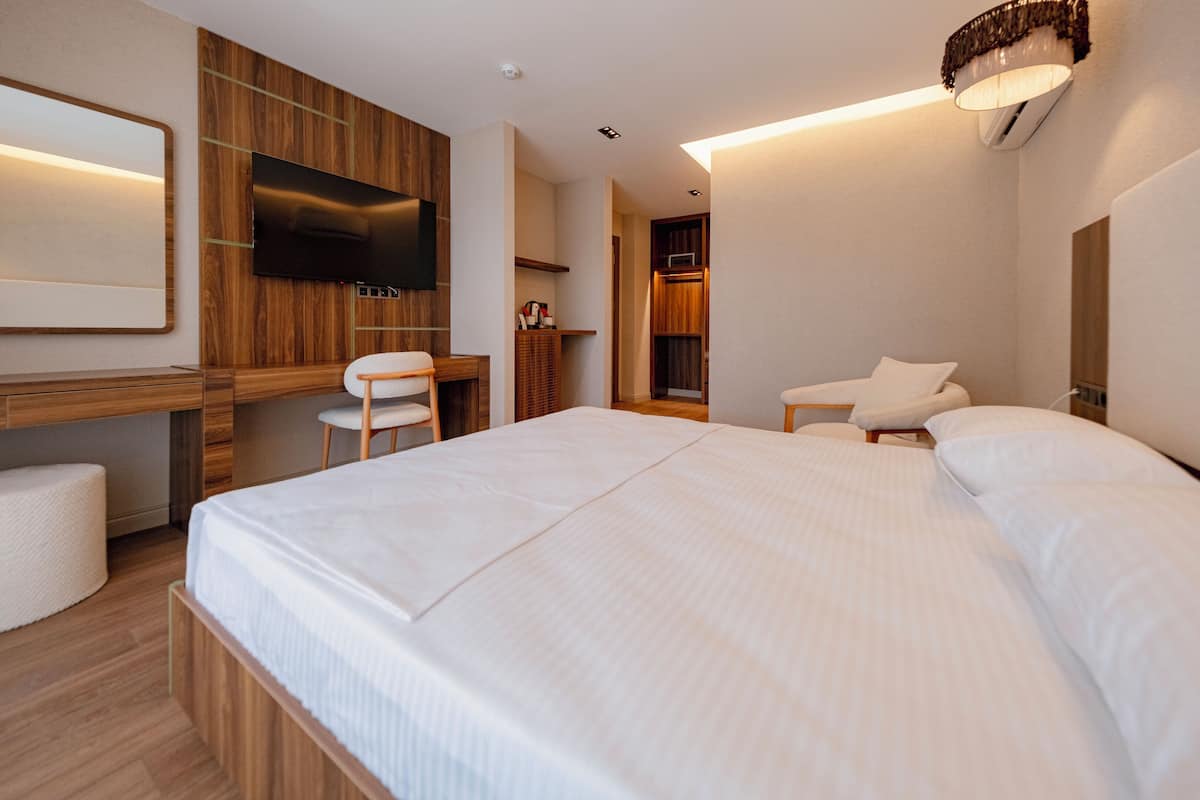 Quarto de hotel moderno com uma cama grande, uma mesa, uma cadeira, uma televisão e um guarda-roupa.