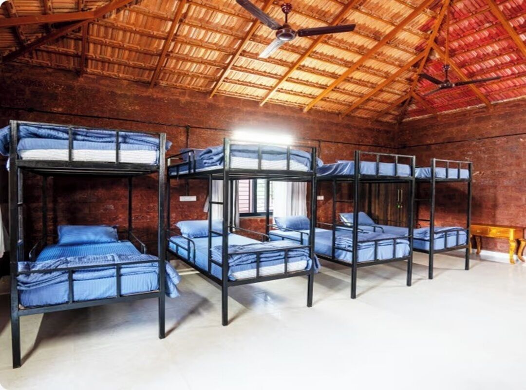 Um dormitório com beliches, um ventilador de teto e uma parede de tijolos.