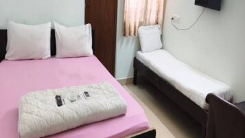 Um quarto com uma cama, mesa de cabeceira, cadeira, televisão e janela com cortinas.