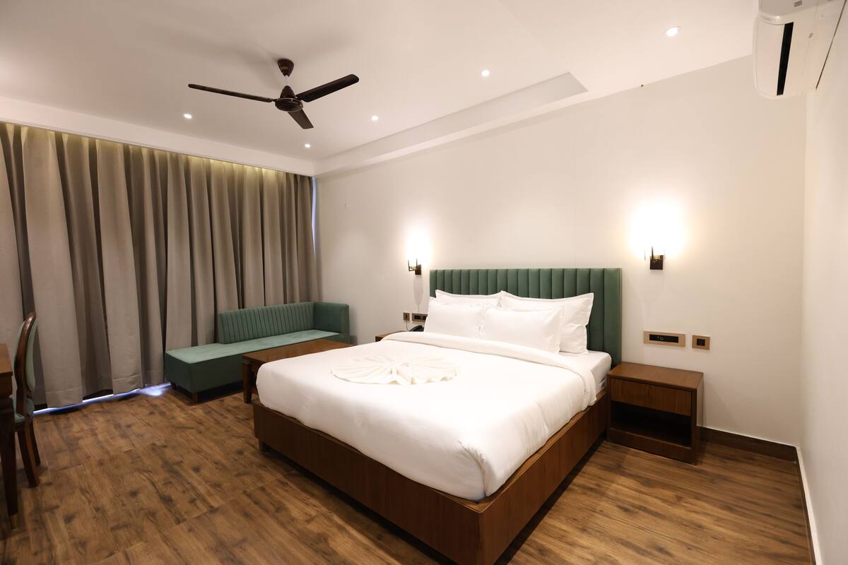 Quarto de hotel moderno com uma cama grande, um ventilador de teto, um sofá verde e uma mesinha de cabeceira.