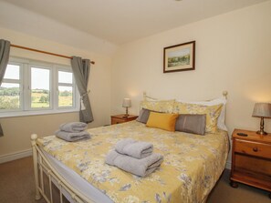 Quarto com cama, mesa de cabeceira, abajur, janela com cortinas e um quadro na parede.
