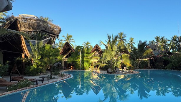 Um resort com piscina cristalina, construções de telhado de palha e vegetação exuberante.