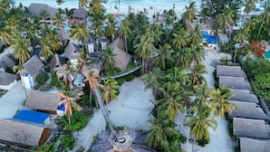 Vista aérea de um resort com chalés de telhado de palha, palmeiras e uma praia.