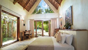 Quarto com uma cama grande, uma escrivaninha e vista para uma piscina e vegetação.