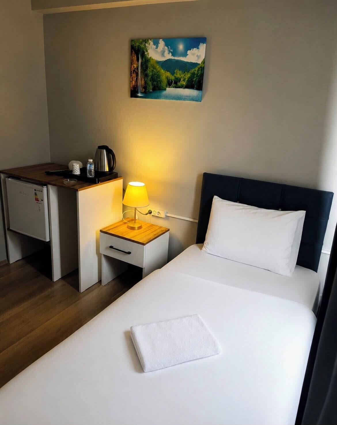 Quarto de hotel com cama, escrivaninha, mesa de cabeceira, luminária, quadro e cafeteira.