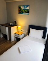 Quarto de hotel com cama, escrivaninha, mesa de cabeceira, luminária, quadro e cafeteira.