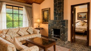 Quarto com sofá, lareira, luminária e cama com vista para o verde lá fora.