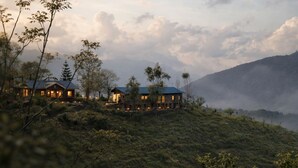 Propriedade numa encosta com vários edifícios, rodeada por árvores e com uma montanha ao fundo.