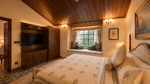 Quarto com cama grande, televisão, armários de madeira, janela com vista e um quadro na parede.