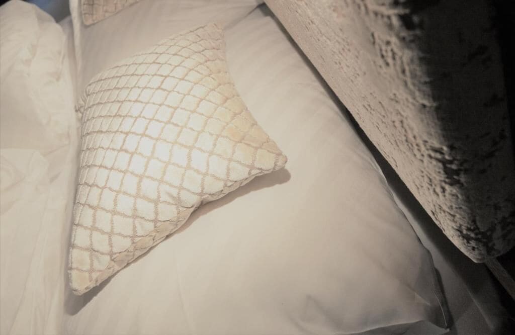Uma cama com travesseiro branco e manta texturizada.