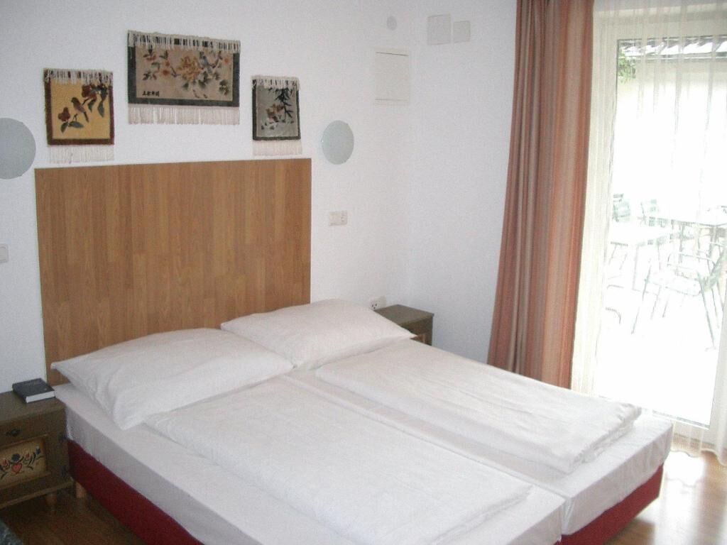 Uma cama de casal com cabeceira de madeira, uma mesa de cabeceira e uma janela com cortinas.