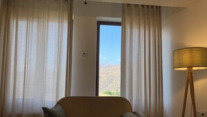 Quarto com sofá, luminária e vista pela janela.