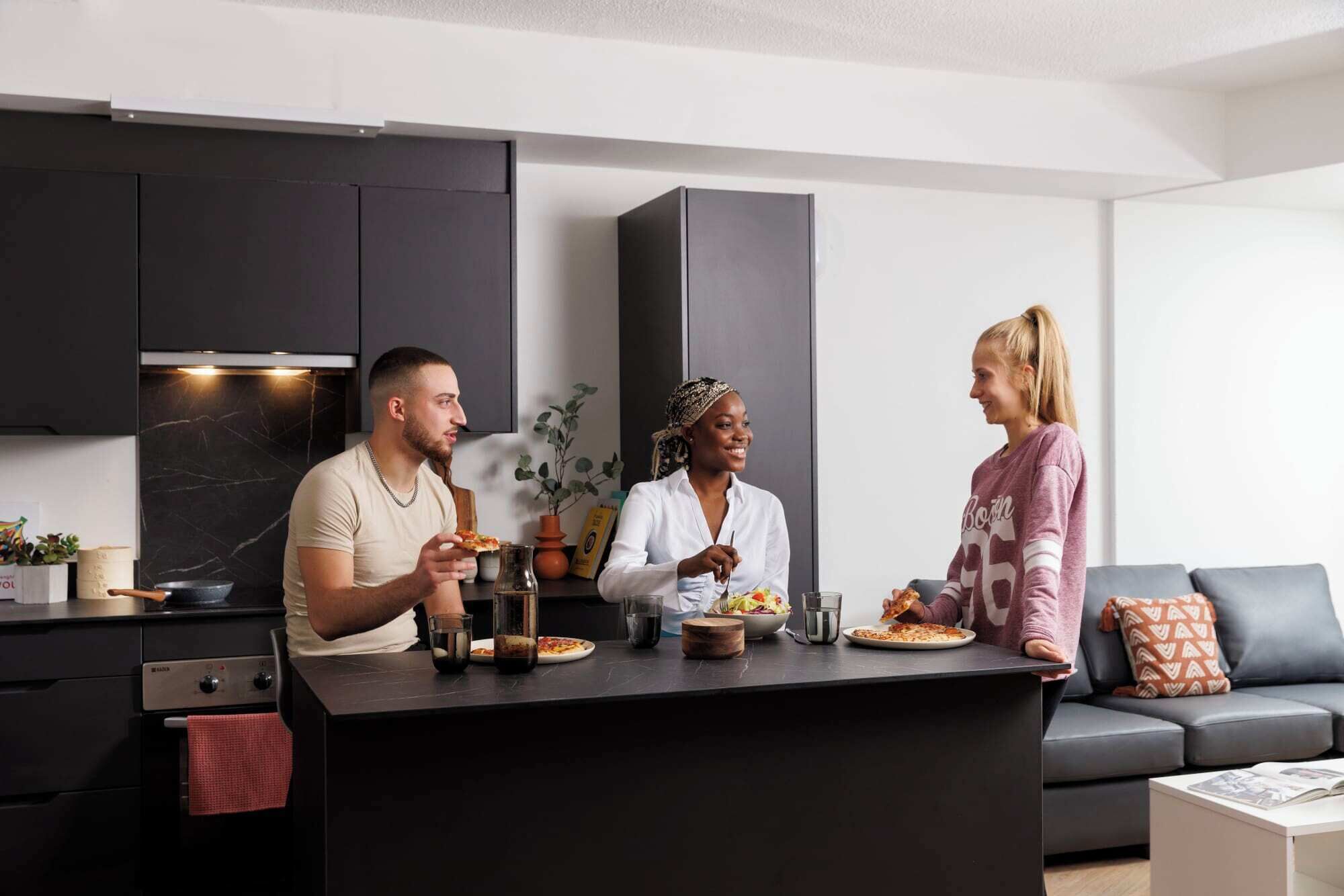 Uma cozinha moderna com armários escuros, uma ilha central e uma área de refeições com um sofá.