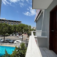 Uma varanda com vista para uma piscina, carros estacionados e um edifício ao fundo.