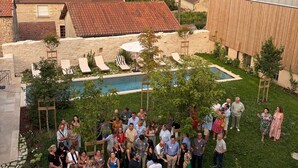 Um grupo de pessoas reunido em um quintal com piscina, cercado por construções de pedra e uma estrutura de madeira.