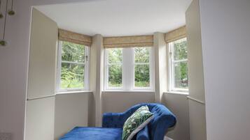 Quarto com cama de canto, duas janelas com cortinas, uma tomada e uma pequena planta.