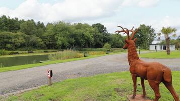 Estátua de um veado em um caminho de cascalho ao lado de uma estrada com placa de limite de velocidade.