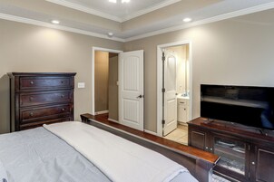 Quarto com cama, cômoda, aparador para TV e duas portas que dão para outros cômodos.