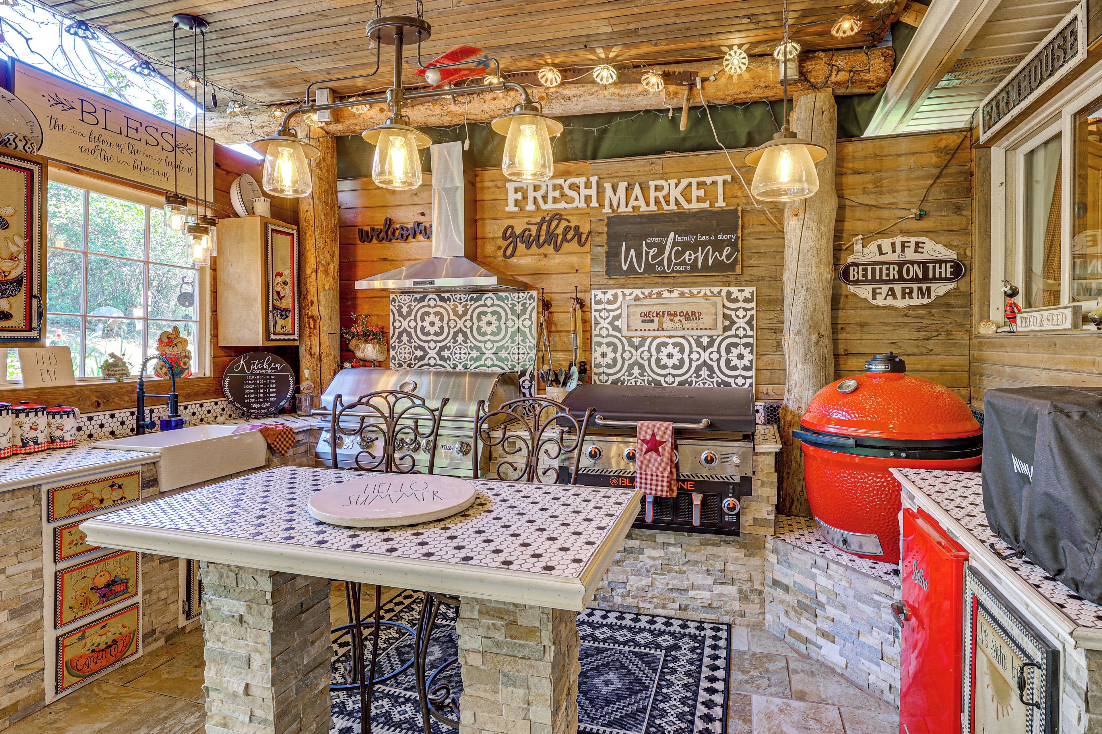 Uma cozinha rústica com azulejos na parede, uma ilha central, luminárias pendentes e uma churrasqueira vermelha grande.