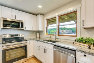 Cozinha moderna com eletrodomésticos de aço inoxidável, armários brancos, uma janela ampla com vista e uma lava-louças embutida.