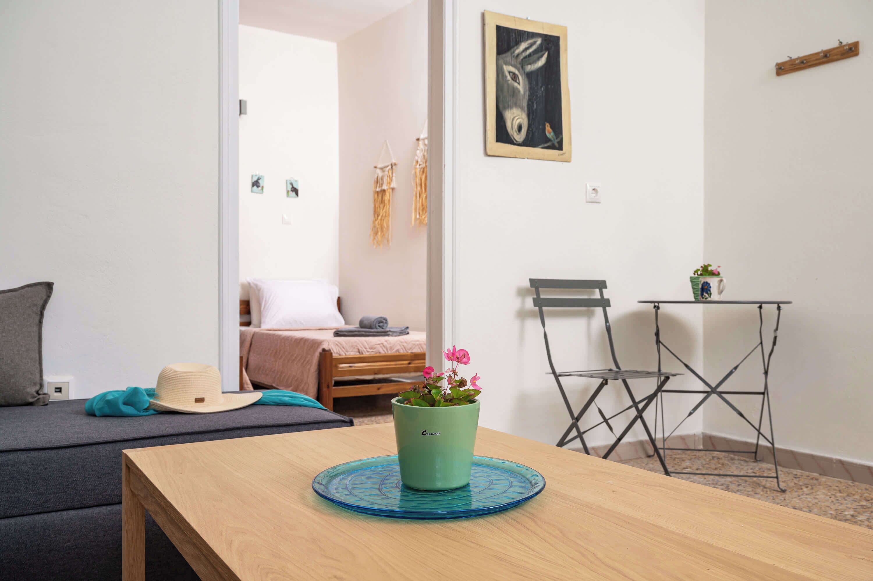 Quarto com cama, uma pequena mesa com planta em vaso, cadeira dobrável e quadro na parede.