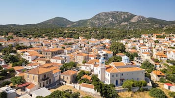 Uma vila costeira com edifícios brancos e telhados vermelhos, rodeada por vegetação e montanhas.